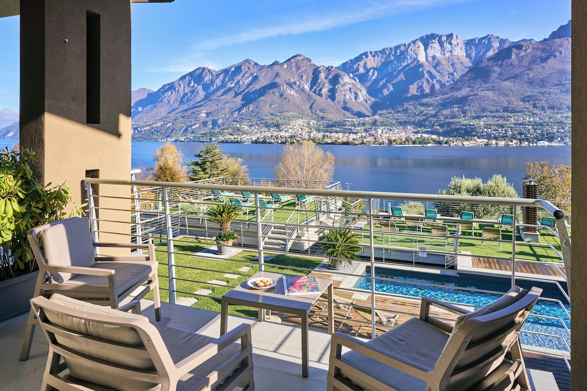 Uma varanda com área de estar externa, piscina e vista para montanhas e um lago.