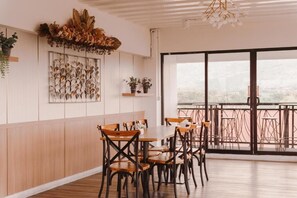 Uma sala de jantar com mesa e cadeiras de madeira, uma parede decorativa com conchas, e uma varanda com vista.