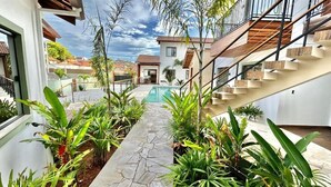 Uma casa moderna com um caminho de pedra que leva a uma piscina, rodeada por vegetação exuberante.