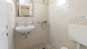 Casa de banho com lavatório, espelho e chuveiro.