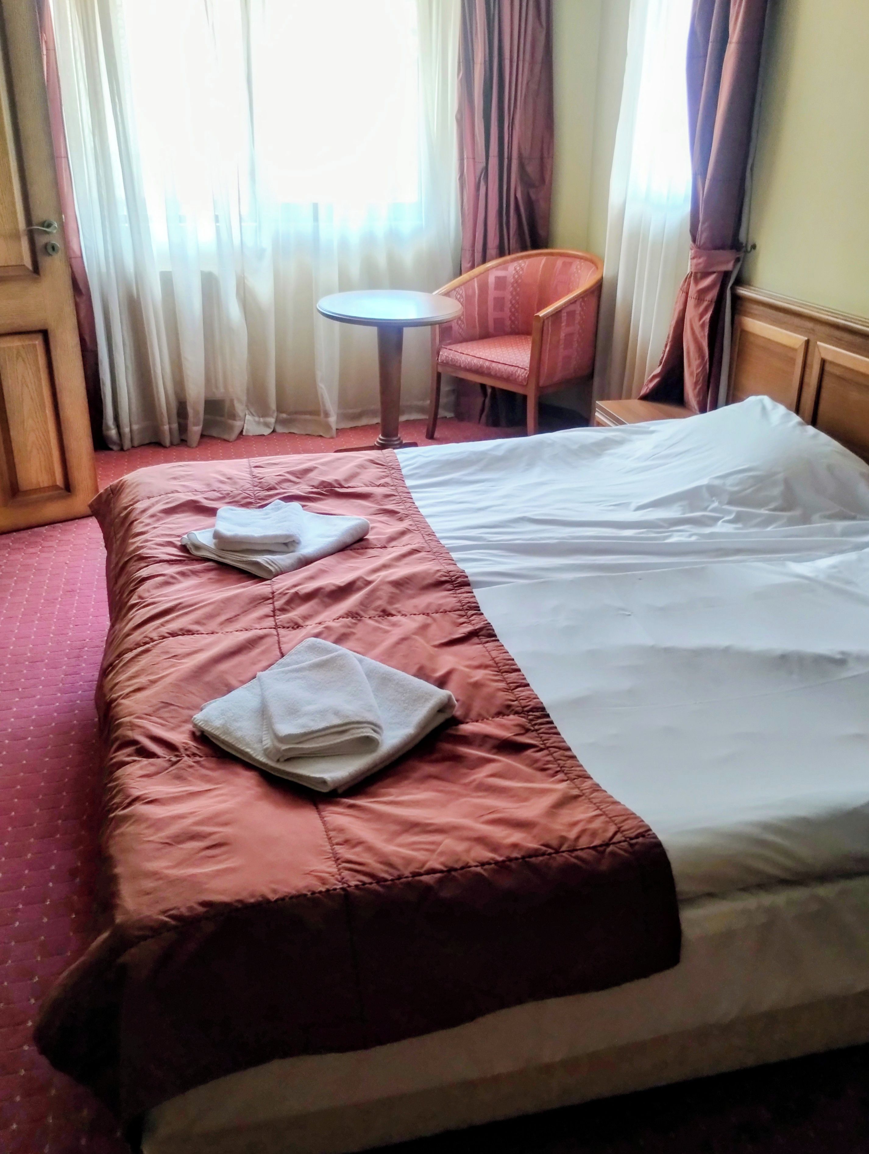 Quarto de hotel com cama, uma cadeira e uma mesinha.