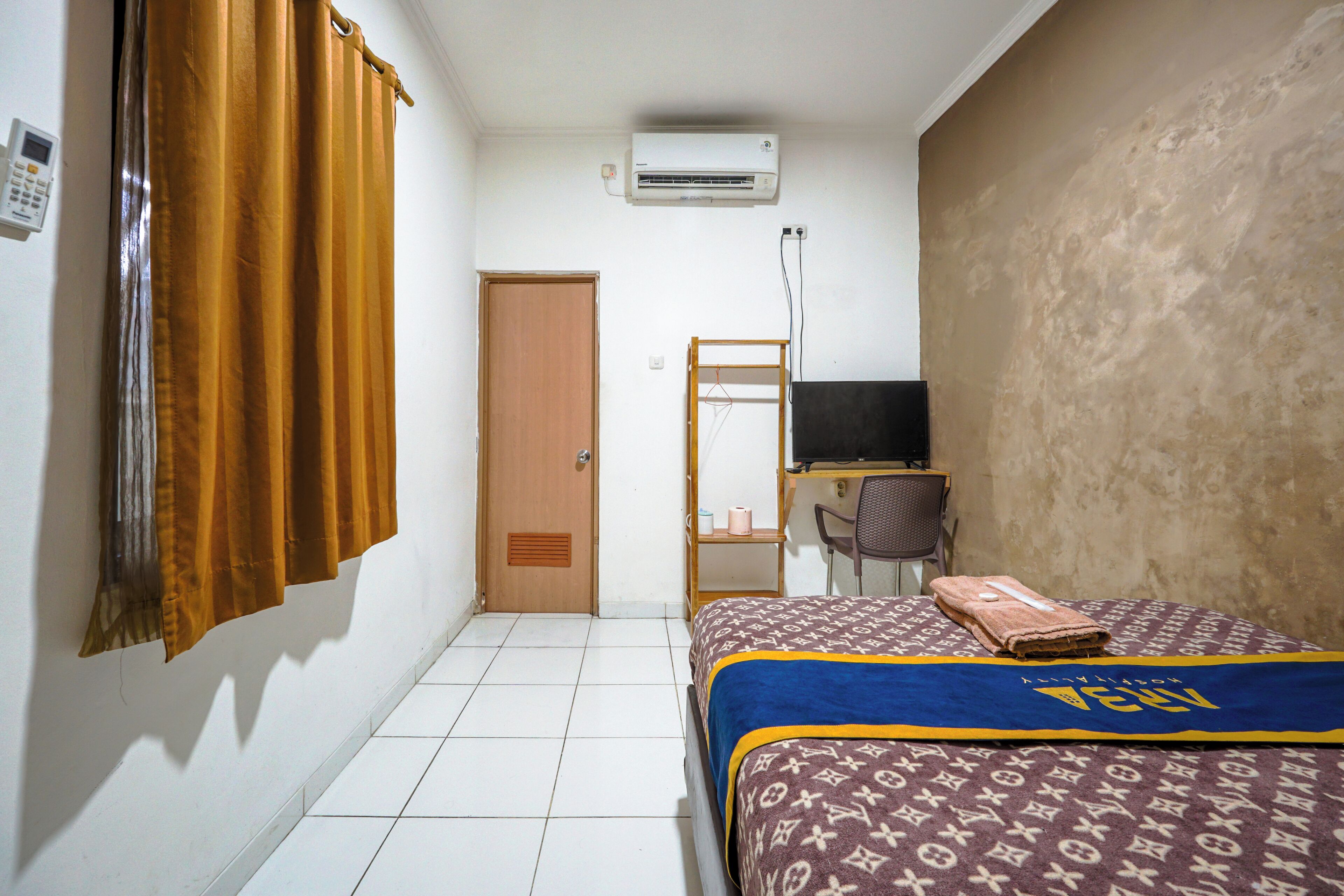 Quarto de hotel com cama, escrivaninha, cadeira, ar condicionado e porta.