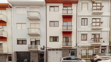 Um edifício residencial com vários andares, varandas, garagem e uma pequena loja no térreo.