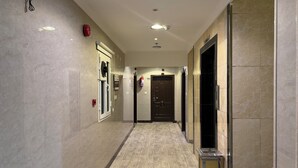 Corredor de hotel com piso de mármore, detector de incêndio e porta com teclado numérico.