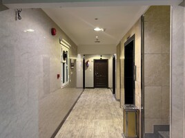 Corredor de hotel com piso de mármore, detector de incêndio e porta com teclado numérico.