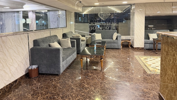 Um hall moderno com sofás cinza, piso de mármore e uma parede de vidro com texto em árabe.