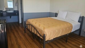 Uma cama de solteiro com cabeceira, mesa de cabeceira, espelho e pia num quarto com piso de madeira.