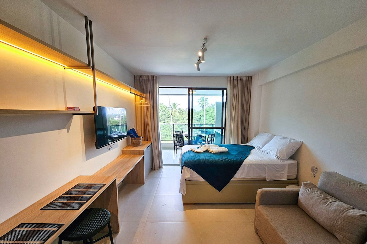 Quarto de hotel com cama, escrivaninha com televisão, sofá e varanda com vista.
