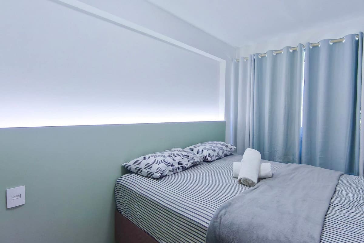 Uma cama de solteiro com roupa de cama listrada, um travesseiro e um cobertor. Há uma tomada na parede.