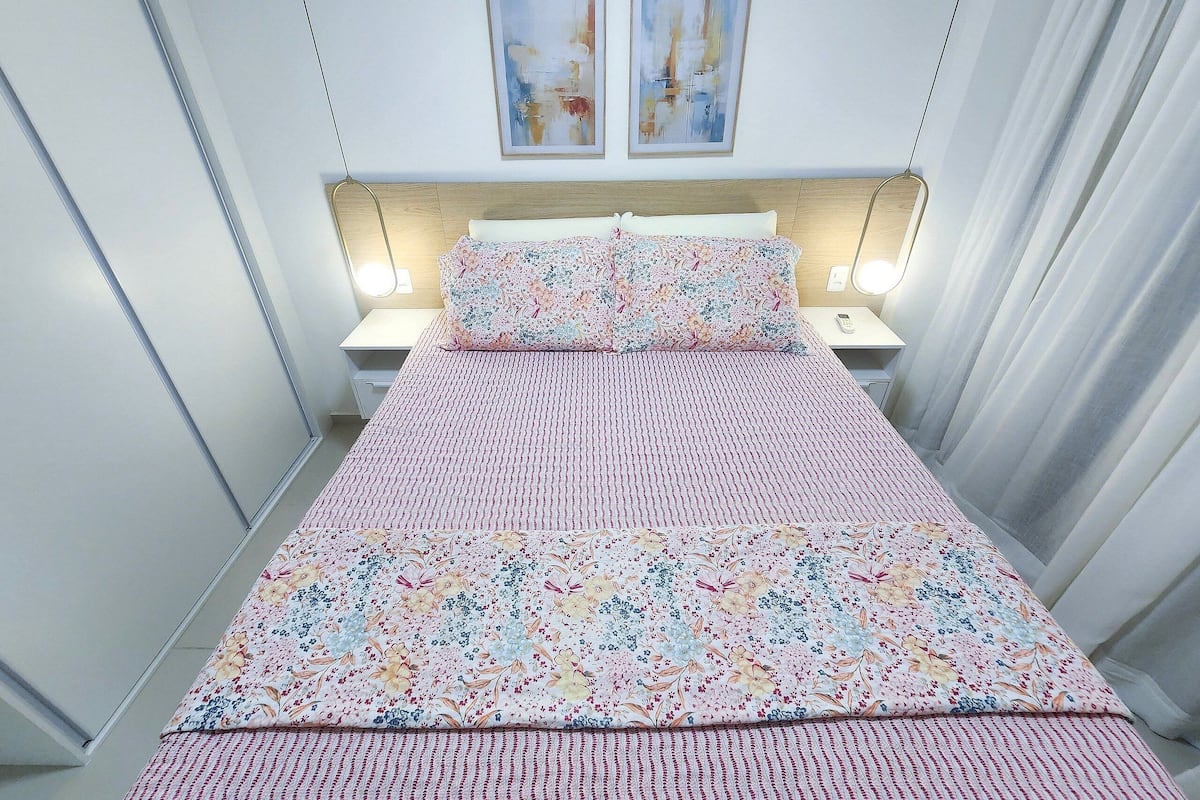 Quarto bem arrumado com uma cama, duas mesas de cabeceira e duas luminárias de parede.