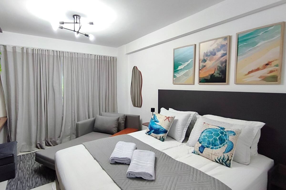 Quarto de hotel moderno com cama, escrivaninha e uma grande janela com cortinas.