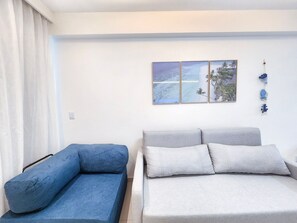 Quarto com um sofá azul e um sofá cinza, uma pintura de uma cena de praia e um objeto decorativo na parede.