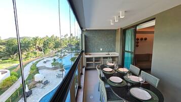 Varanda com mesa de jantar posta para dois, com vista para uma piscina e vegetação exuberante.