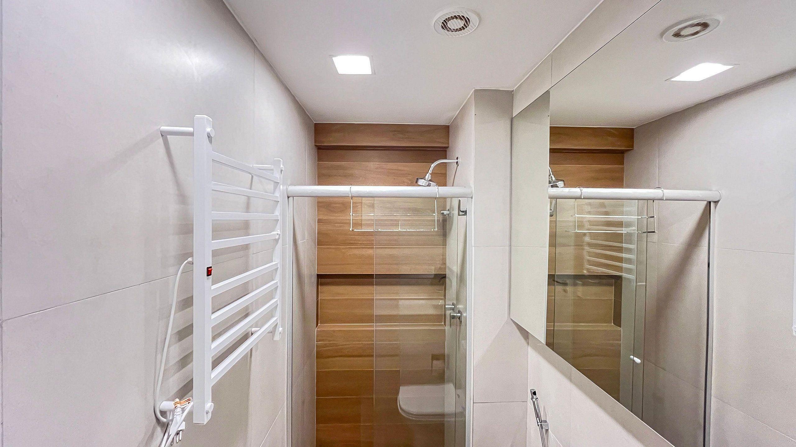 Um banheiro moderno com box de vidro, porta-toalhas branco e toucador de madeira.