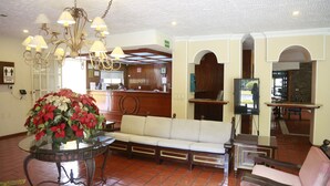 Um hall de entrada com sofá, cadeiras, uma mesa com arranjo floral, um lustre e uma televisão.