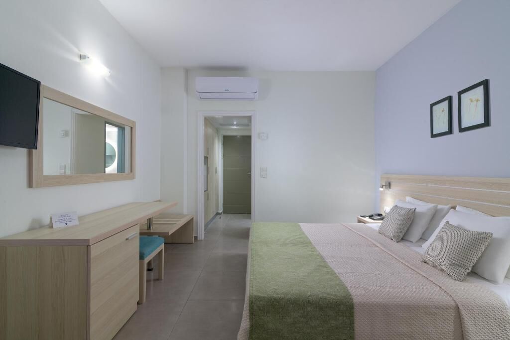 Quarto de hotel com cama, escrivaninha, cadeira, espelho e televisão.