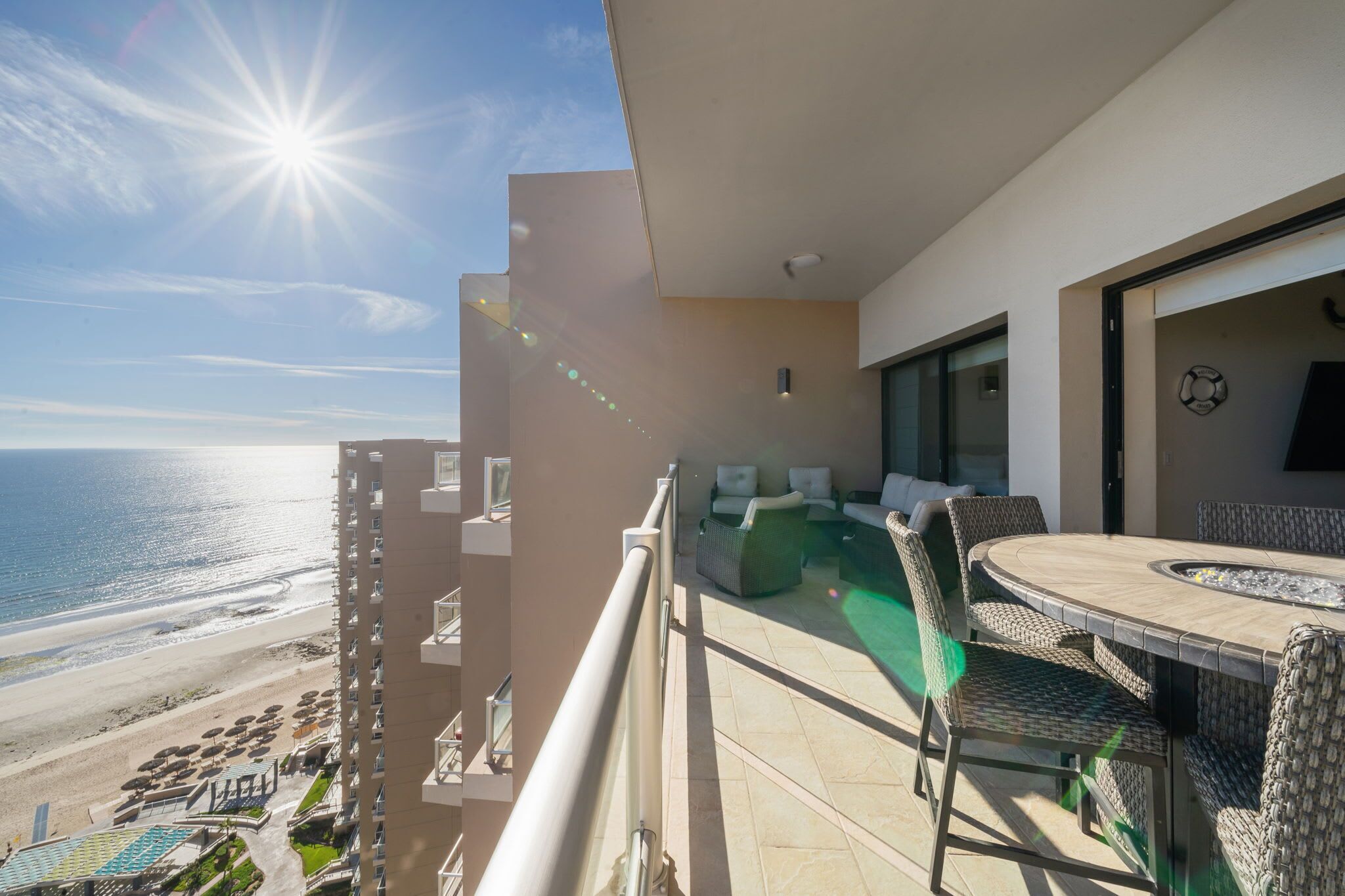 Uma varanda com vista para a praia, uma mesa redonda com cadeiras e um sofá.