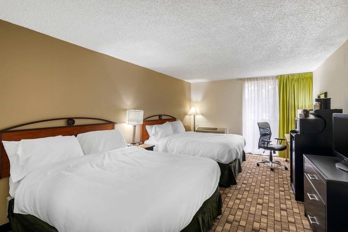 Quarto de hotel com duas camas, uma escrivaninha, uma cadeira e uma televisão.