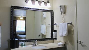 Casa de banho com um espelho grande, pia, secador de cabelo e porta-toalhas.