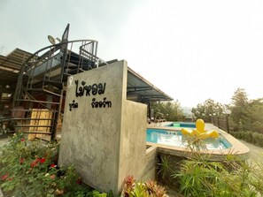 Uma estrutura de concreto com piscina e boias infláveis, cercada por vegetação e um edifício com escada de metal.