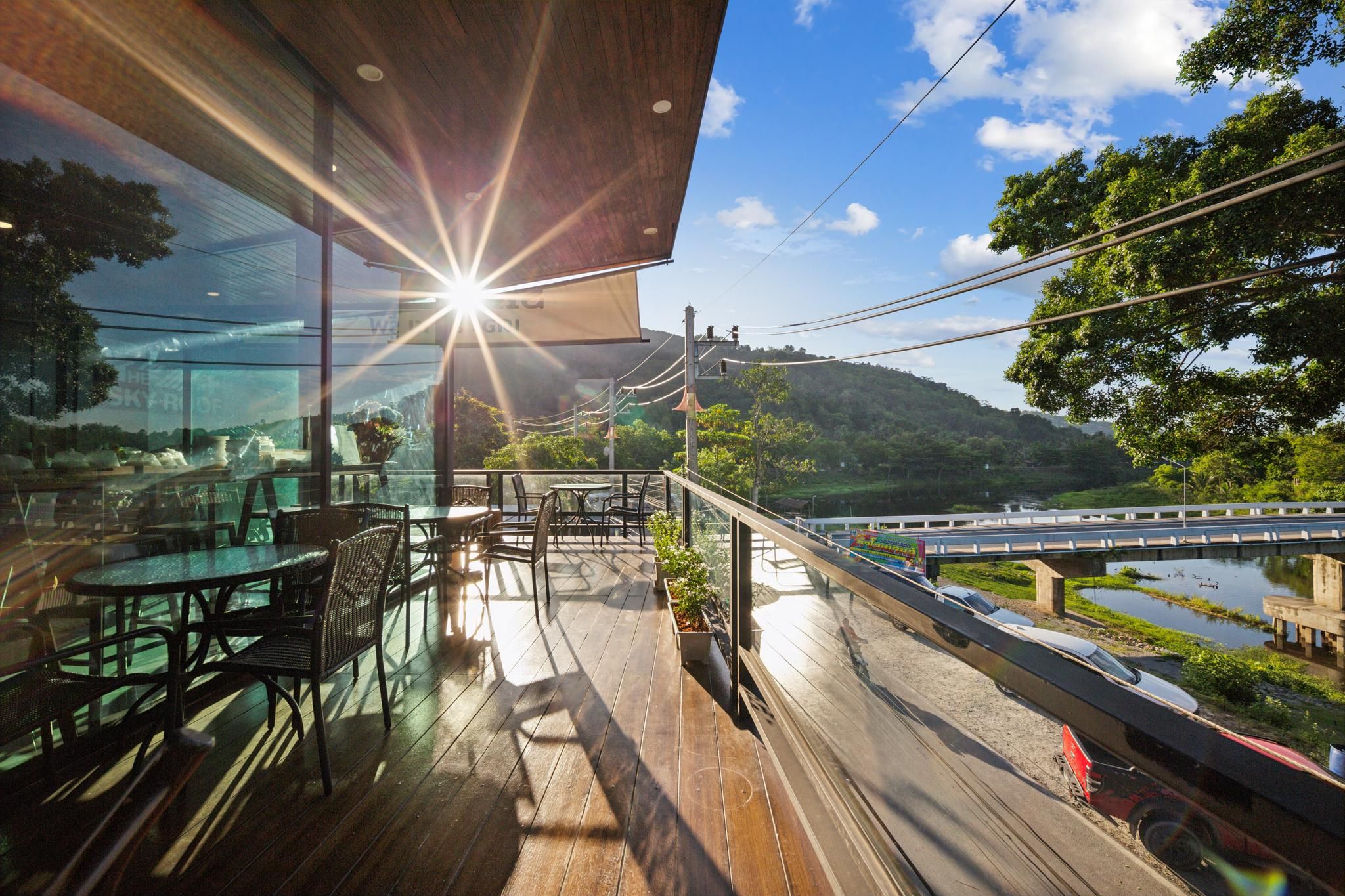 Varanda com mesas e cadeiras, com vista para um rio e uma ponte.