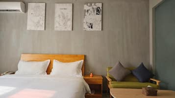 Quarto de hotel com cama de madeira, sofá verde, mesinha e três obras de arte na parede.