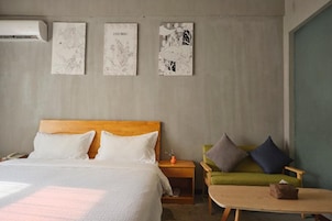 Quarto de hotel com cama de madeira, sofá verde, mesinha e três obras de arte na parede.