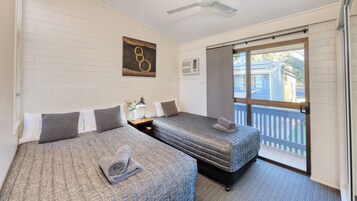 Quarto de hotel com duas camas, ventoinha no teto, janela com vista para o exterior e ar condicionado fixado na parede.