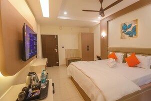 Quarto de hotel com cama, televisão na parede, ventoinha no teto e um quadro na parede.