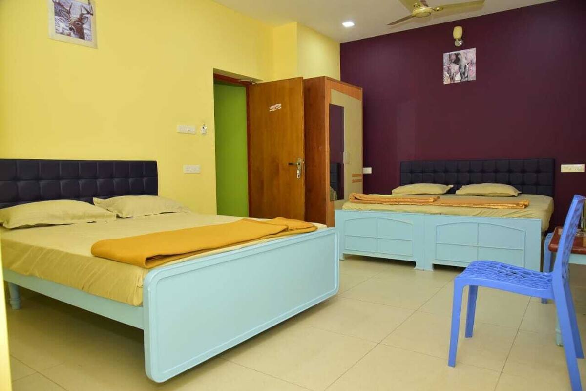 Quarto com duas camas, uma cadeira azul e um ventilador de teto.