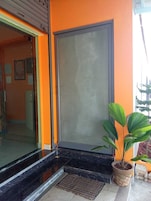 Entrada de um edifício com porta de vidro, planta em vaso e tapete de entrada.