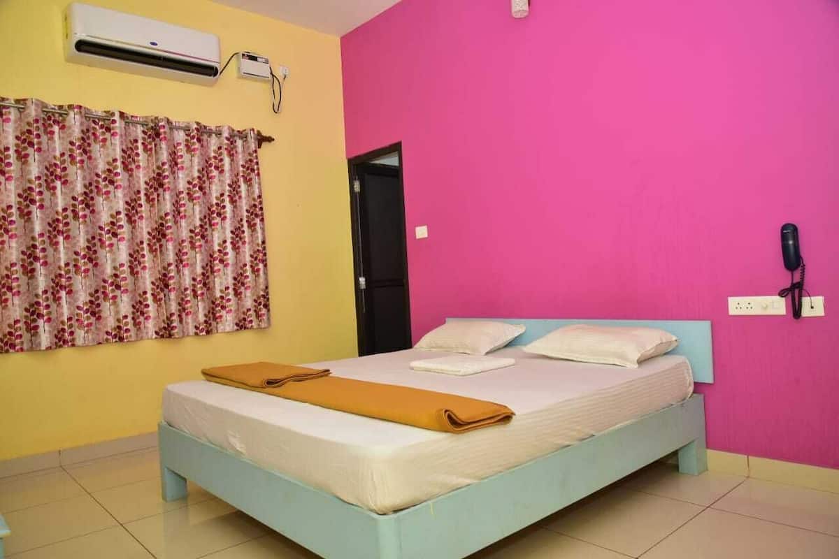 Quarto com cama, cortina, ar-condicionado e telefone na parede.