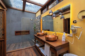 Casa de banho com toucador de madeira, duas pias de cobre, um espelho e um secador de cabelo.