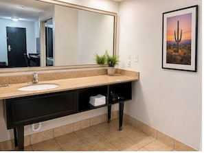 Casa de banho com lavatório, espelho e um quadro de cactos.
