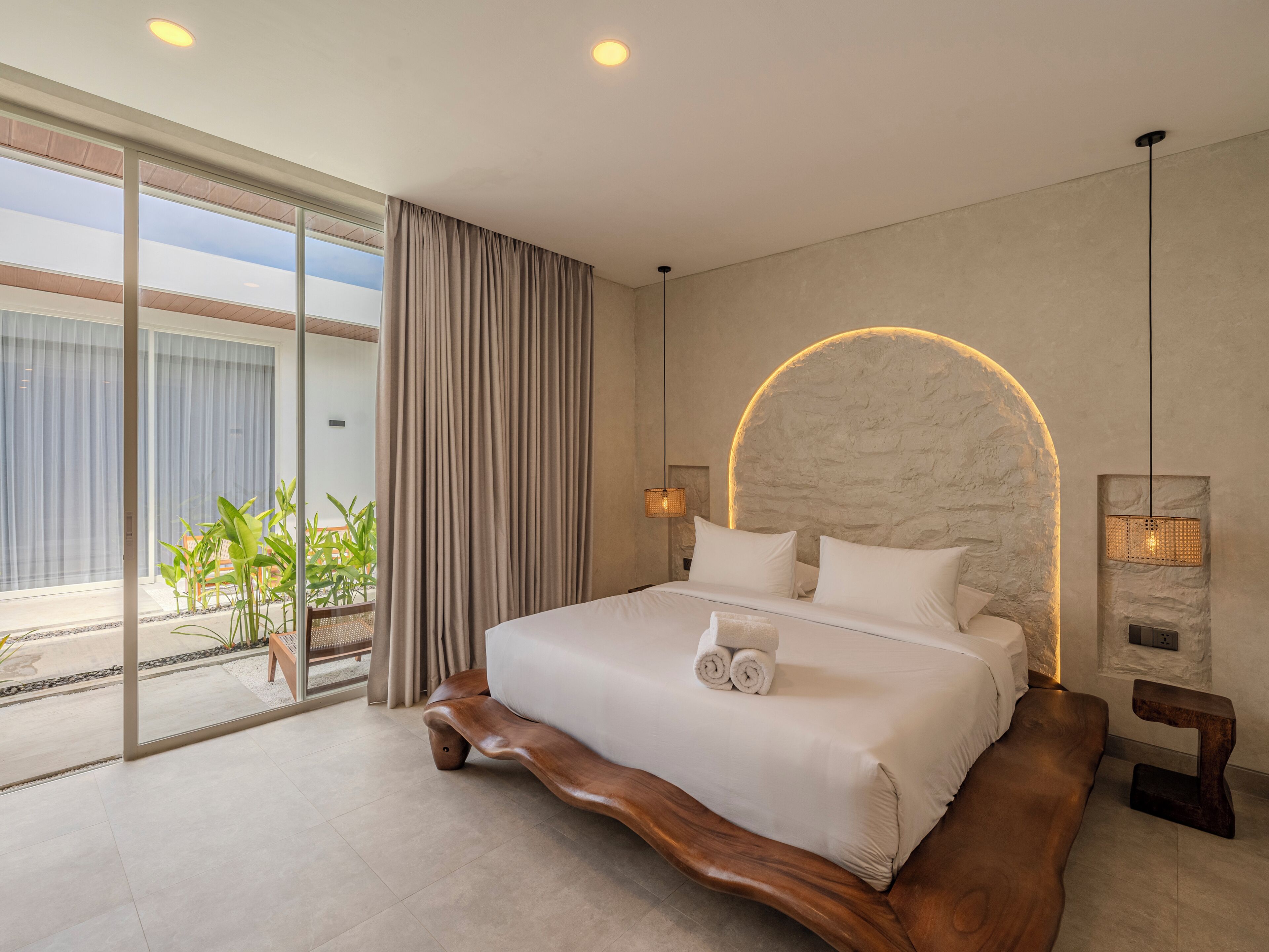 Quarto moderno com uma cama grande, parede de pedra e vista para o verde lá fora.