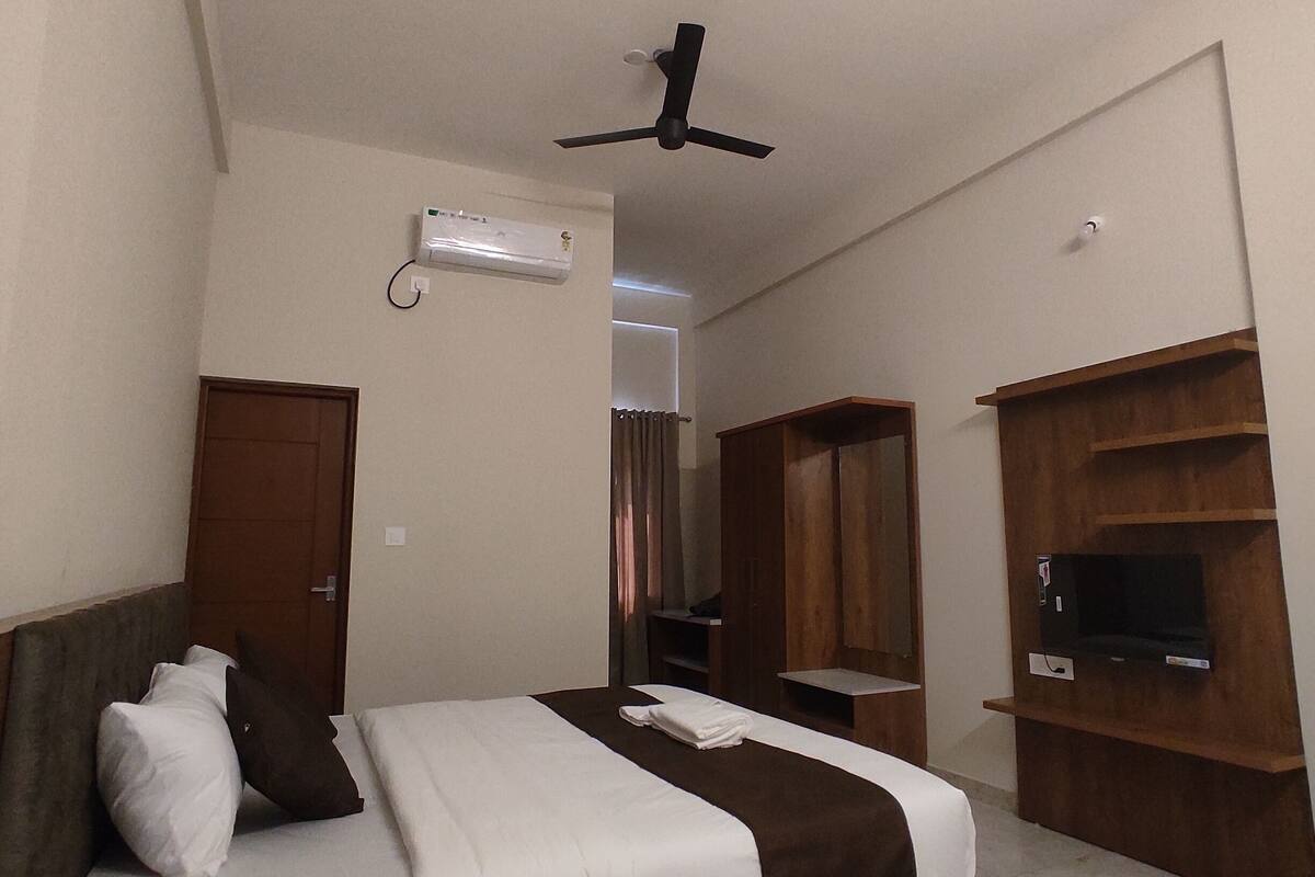 Quarto de hotel com cama, ventoinha no teto, ar condicionado, guarda-roupa de madeira e televisão.