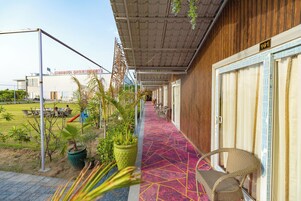 Corredor de hotel com carpete colorido, plantas em vasos e cadeiras de vime.