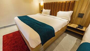 Cama bem arrumada com manta azul-turquesa, cabeceira de madeira e mesa de cabeceira com um telefone.