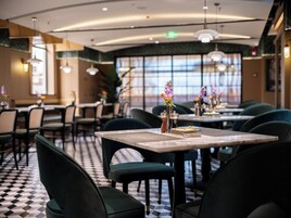 Um restaurante com chão xadrez, cadeiras estofadas verde escuro e mesas decoradas com centros de mesa.
