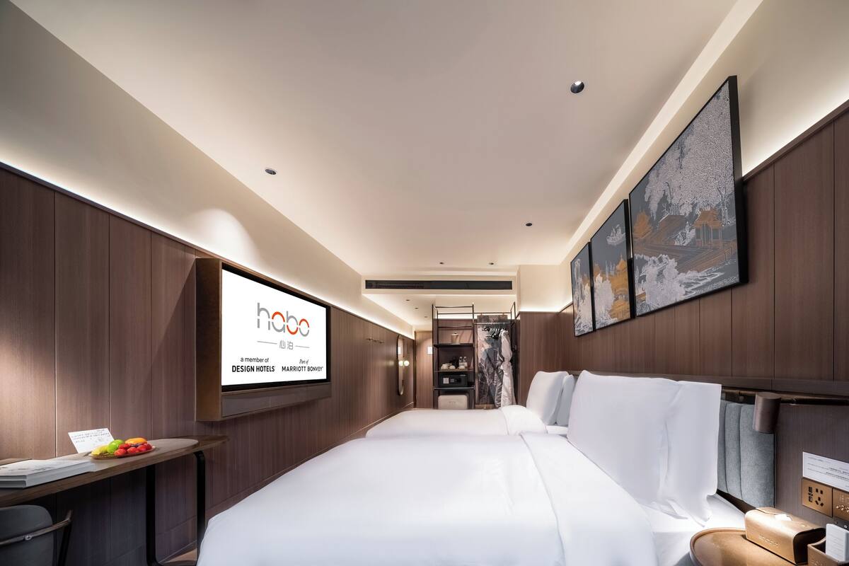 Quarto de hotel com cama, secretária com computador, televisão e obras de arte nas paredes.