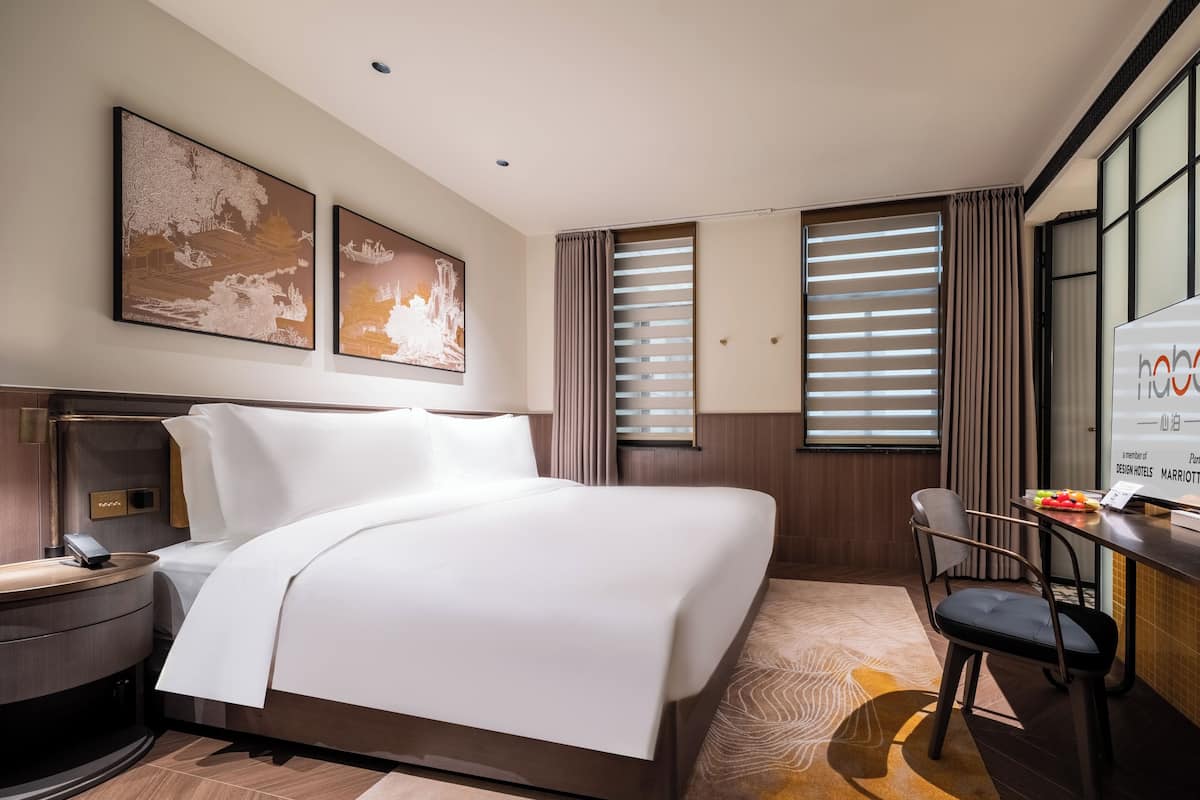 Quarto de hotel com uma cama grande, uma escrivaninha com cadeira, televisão e obras de arte na parede.