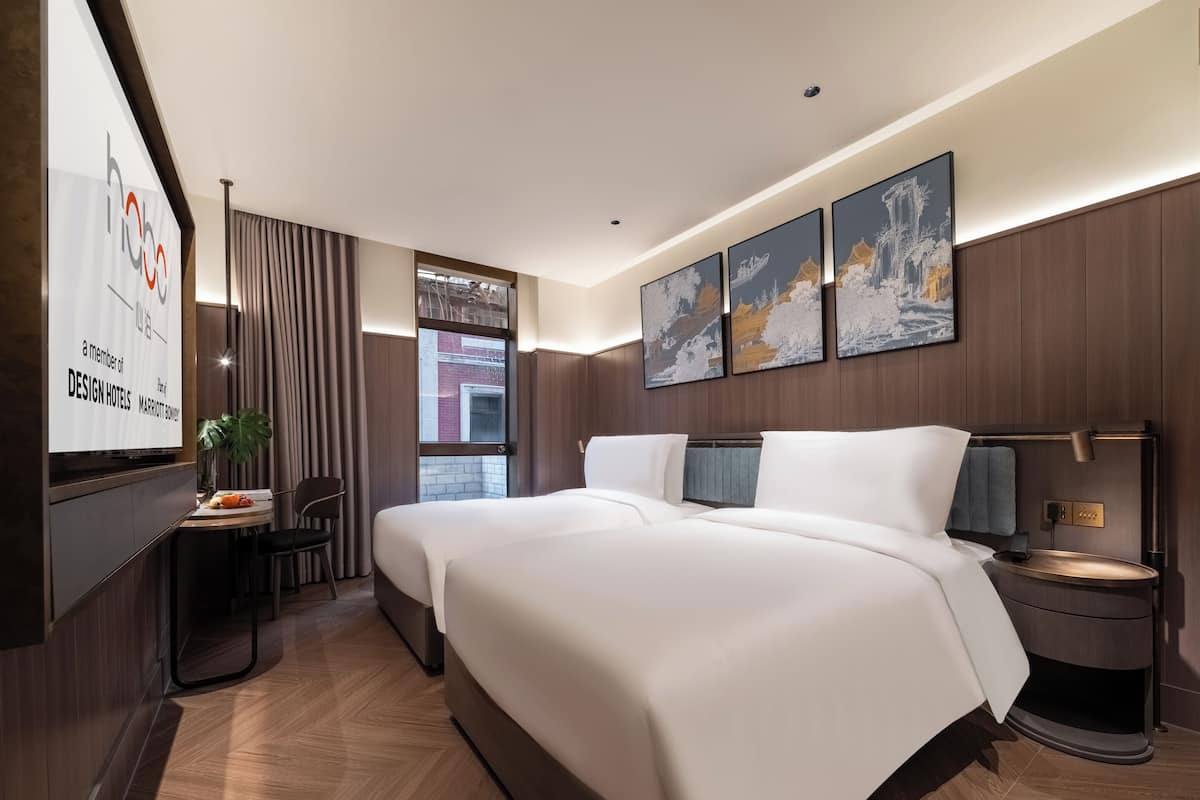 Quarto de hotel moderno com uma cama grande, uma mesa com planta, uma televisão e arte na parede.