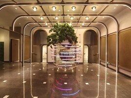 Um lobby com uma árvore decorativa central, piso refletivo e design moderno no teto.