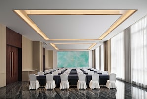 Uma sala de conferência com uma mesa comprida, cadeiras brancas e uma tela grande na frente.