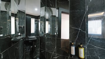 Casa de banho moderna com paredes de mármore preto, um secador de cabelo e duas garrafas de champô.