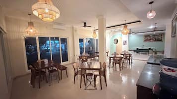 Uma sala de jantar ampla com várias mesas e cadeiras, janelas grandes e luminárias pendentes.