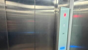 Elevador metálico com painel de controle, botões e um indicador luminoso vermelho.