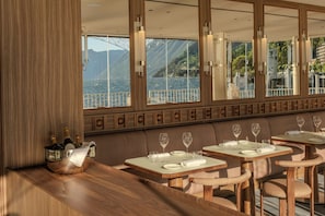 Um restaurante com mobiliário de madeira, grandes janelas e vista para o mar.