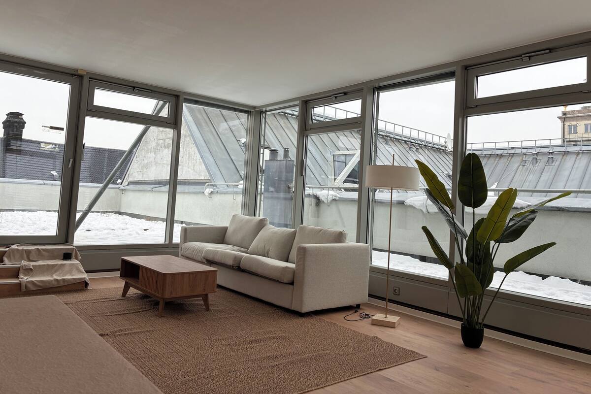 Sala de estar moderna com sofá, mesa de centro e grandes janelas com vista para uma paisagem urbana nevada.