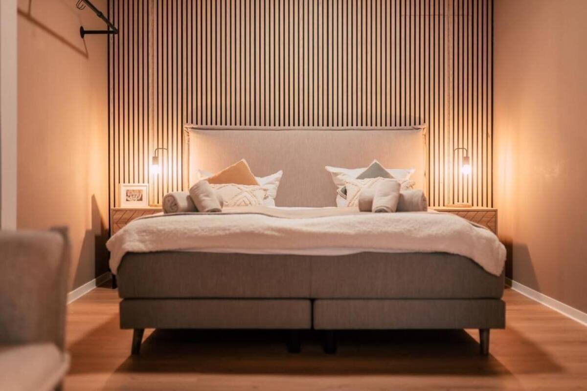 Quarto moderno com uma cama grande, duas mesas de cabeceira e um design de parede ripada.